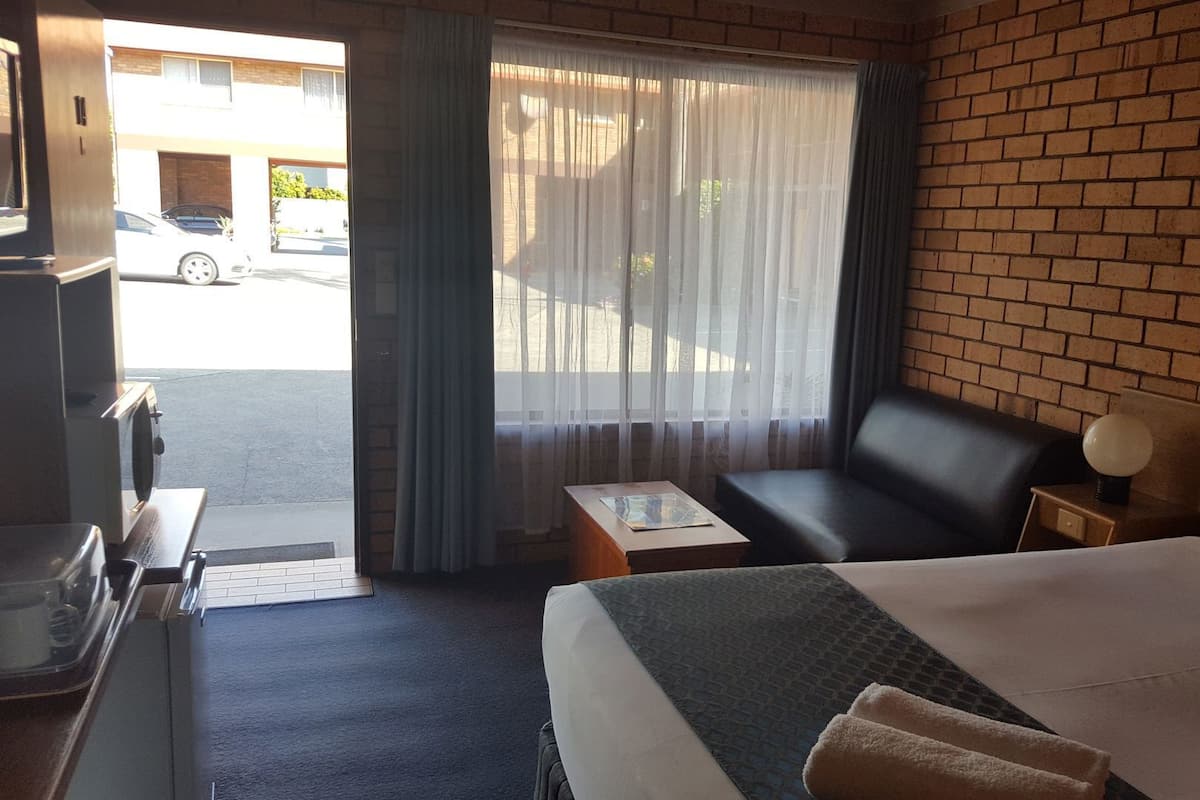 Quarto de hotel com cama, escrivaninha, cadeira, televisão e janela com cortinas.