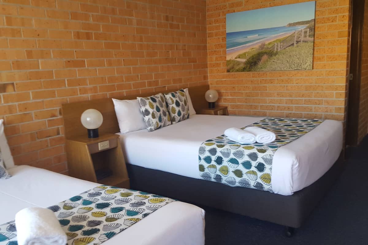 Quarto de hotel com duas camas, parede de tijolos e uma pintura com vista para a praia.