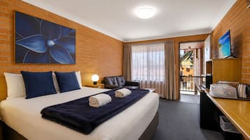 Quarto de hotel com cama, escrivaninha, cadeira, televisão e uma grande janela.