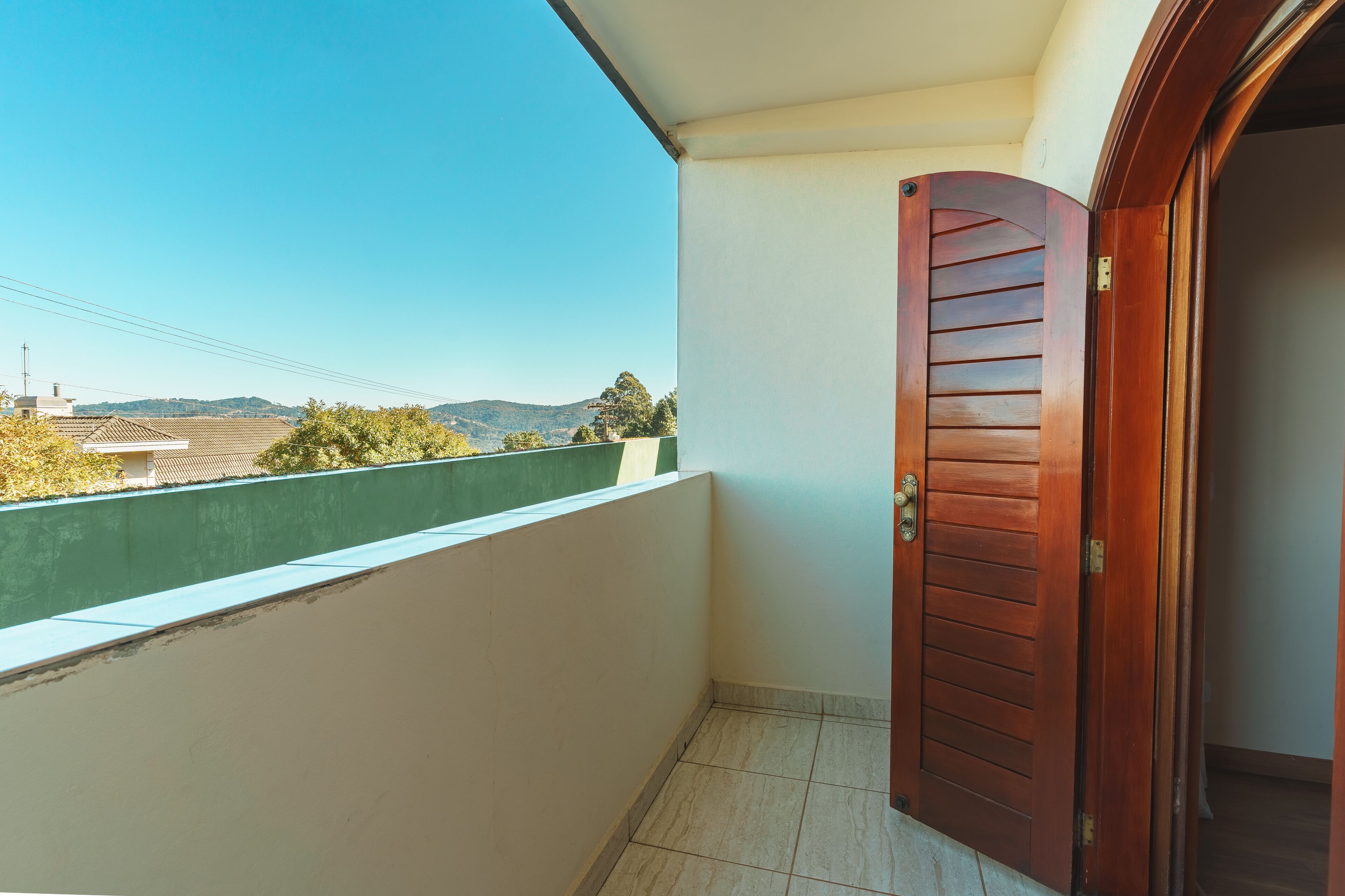 Uma varanda com vista para colinas distantes, uma porta de madeira e um chão de azulejos.