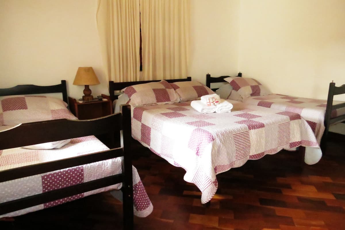 Quarto com duas camas, cada uma com colcha xadrez e almofadas. Um criado-mudo com abajur fica entre as camas.
