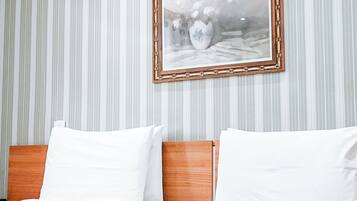Quarto de hotel com uma cama, almofadas brancas, cabeceira de madeira e uma pintura floral emoldurada na parede.