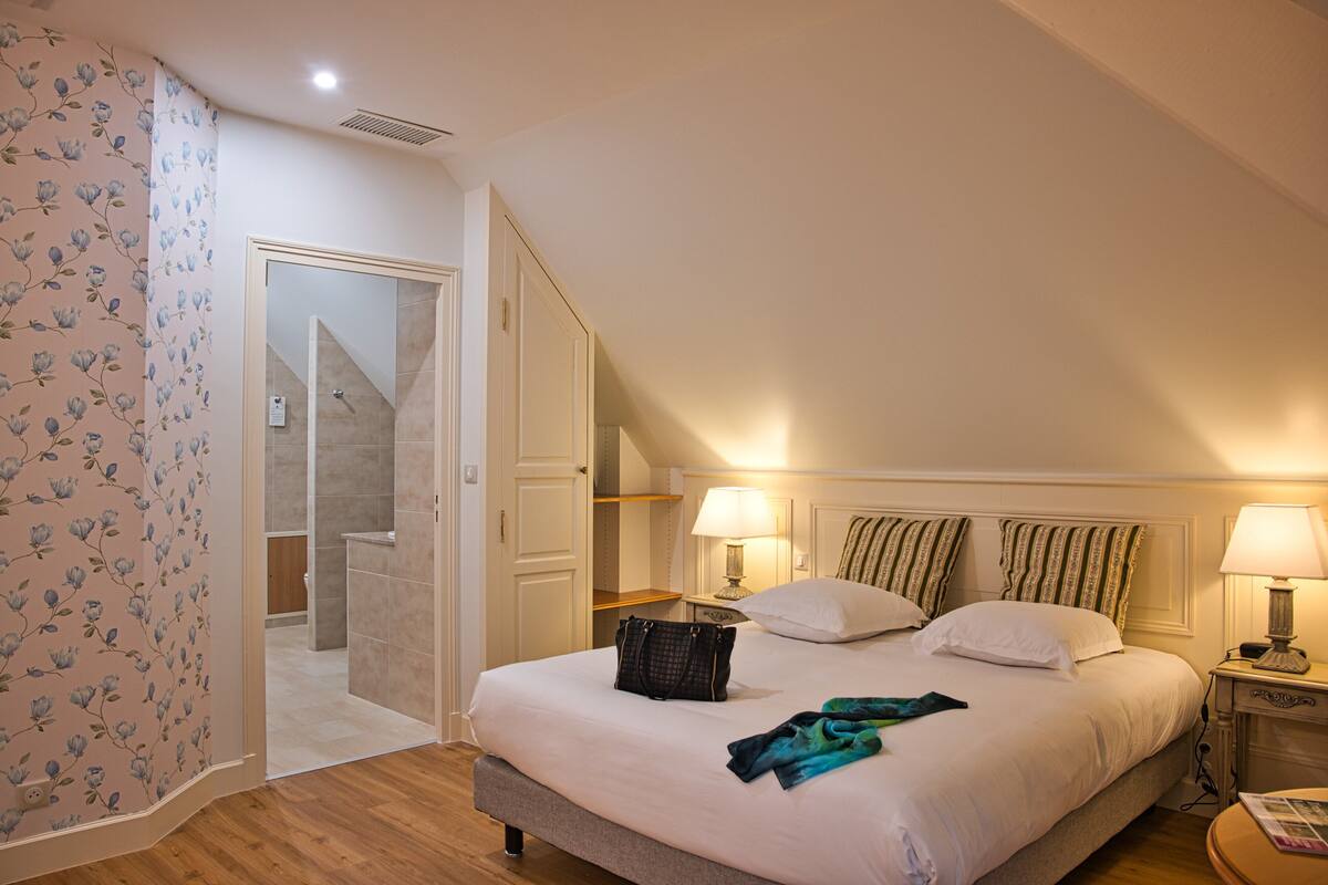 Quarto com uma cama grande, duas luminárias de cabeceira, uma mesa de cabeceira e uma porta para um banheiro.
