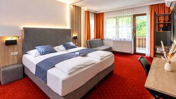 Quarto de hotel com cama, sofá, mesa de jantar e vista para o verde lá fora.