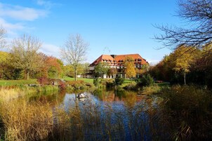 Um hotel com telhado vermelho, rodeado por folhagem outonal e um lago.