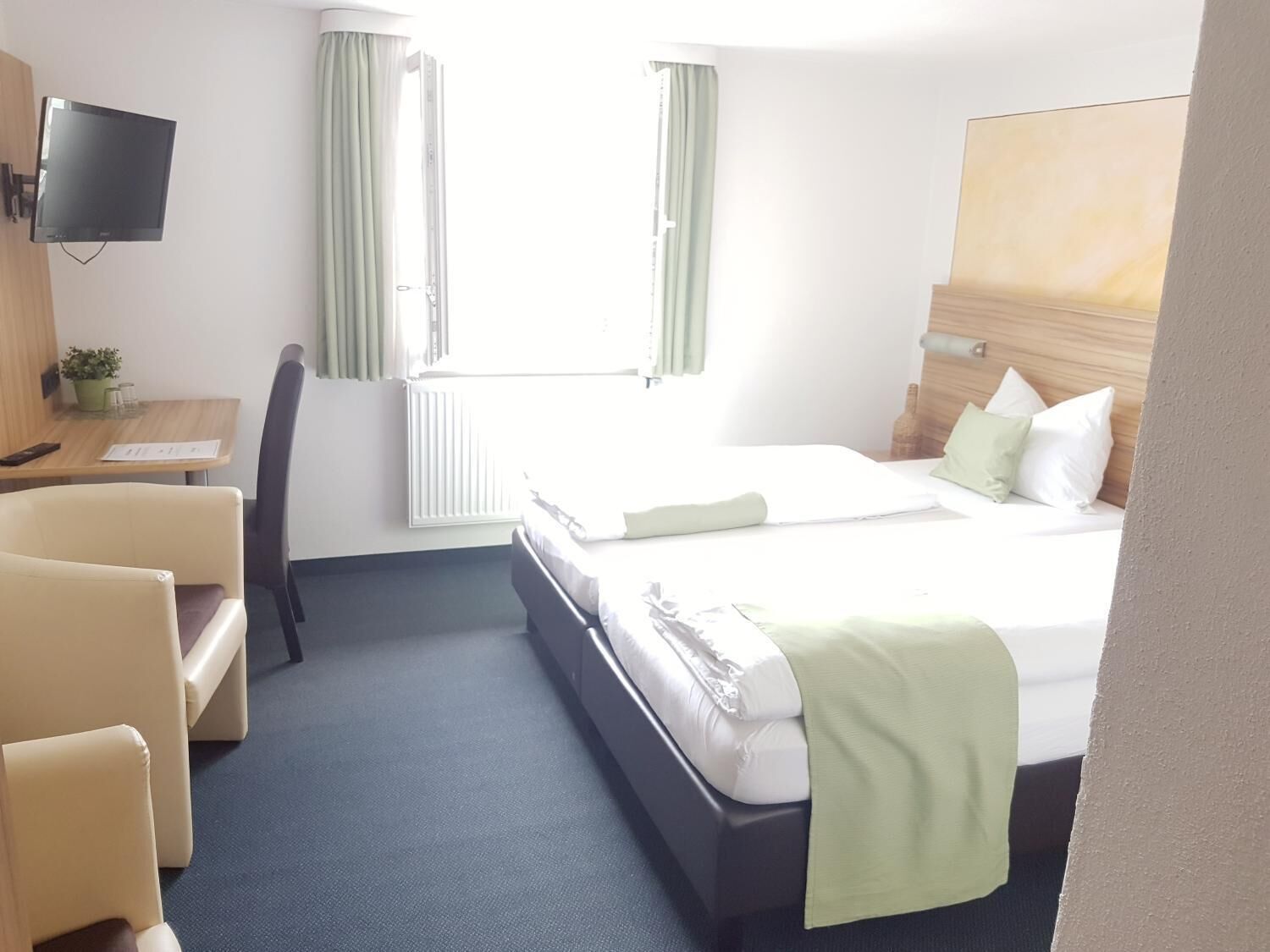 Quarto de hotel com cama, escrivaninha, cadeira, televisão e janela com cortinas.