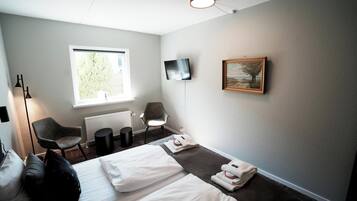 Quarto de hotel com duas camas, uma TV fixada na parede, uma janela com vista para árvores e um quadro na parede.