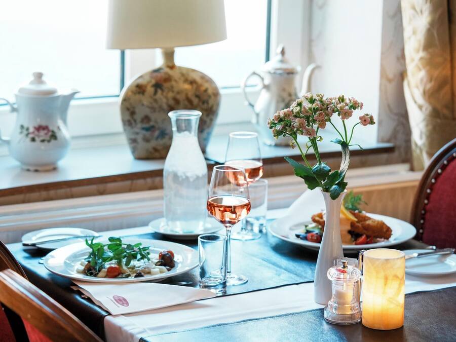 Uma mesa de jantar posta com pratos, copos, uma vela e um vaso com flores.