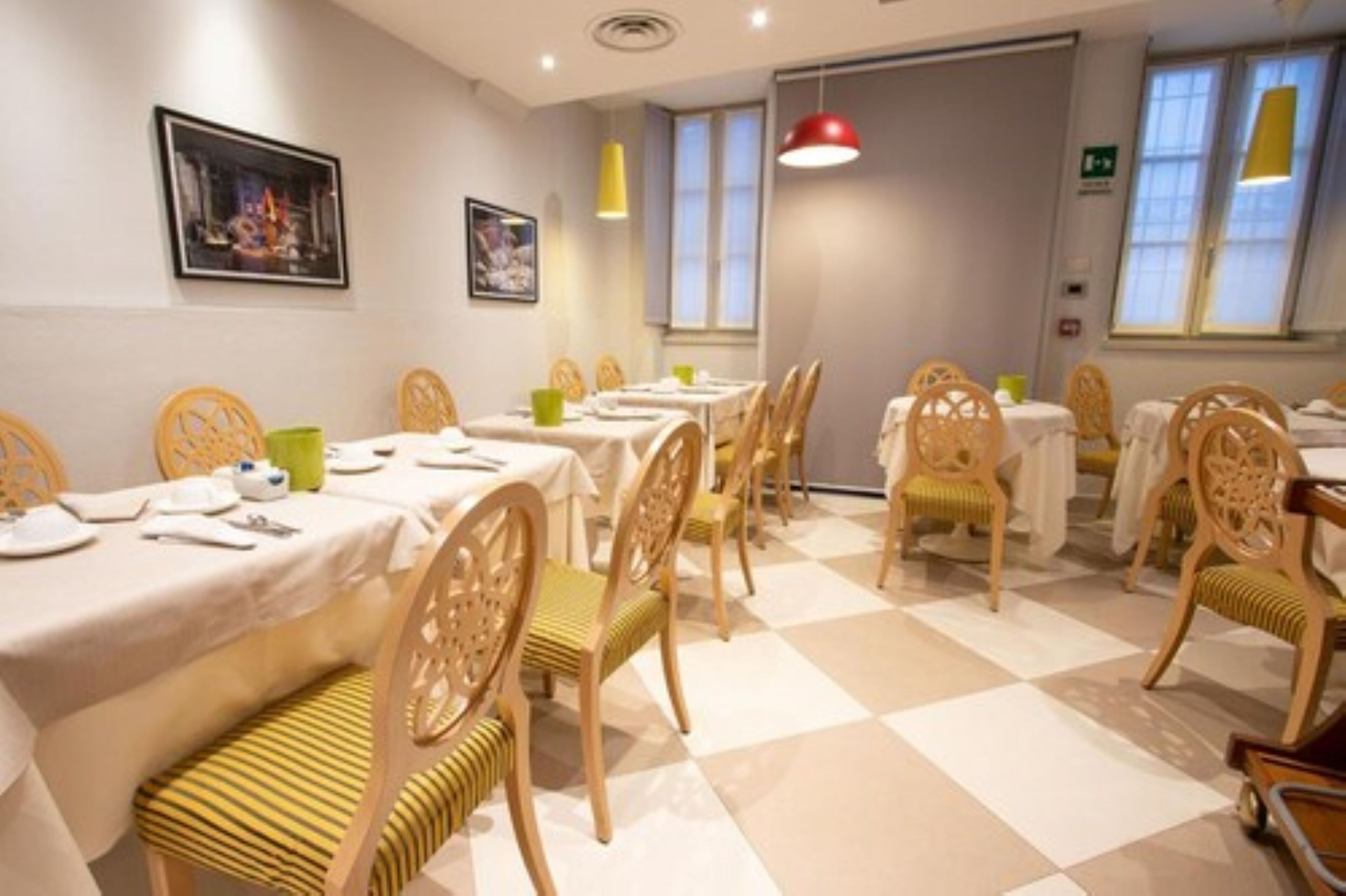 Uma sala de jantar com várias mesas e cadeiras, dispostas num ambiente amplo com padrão de tabuleiro quadriculado.