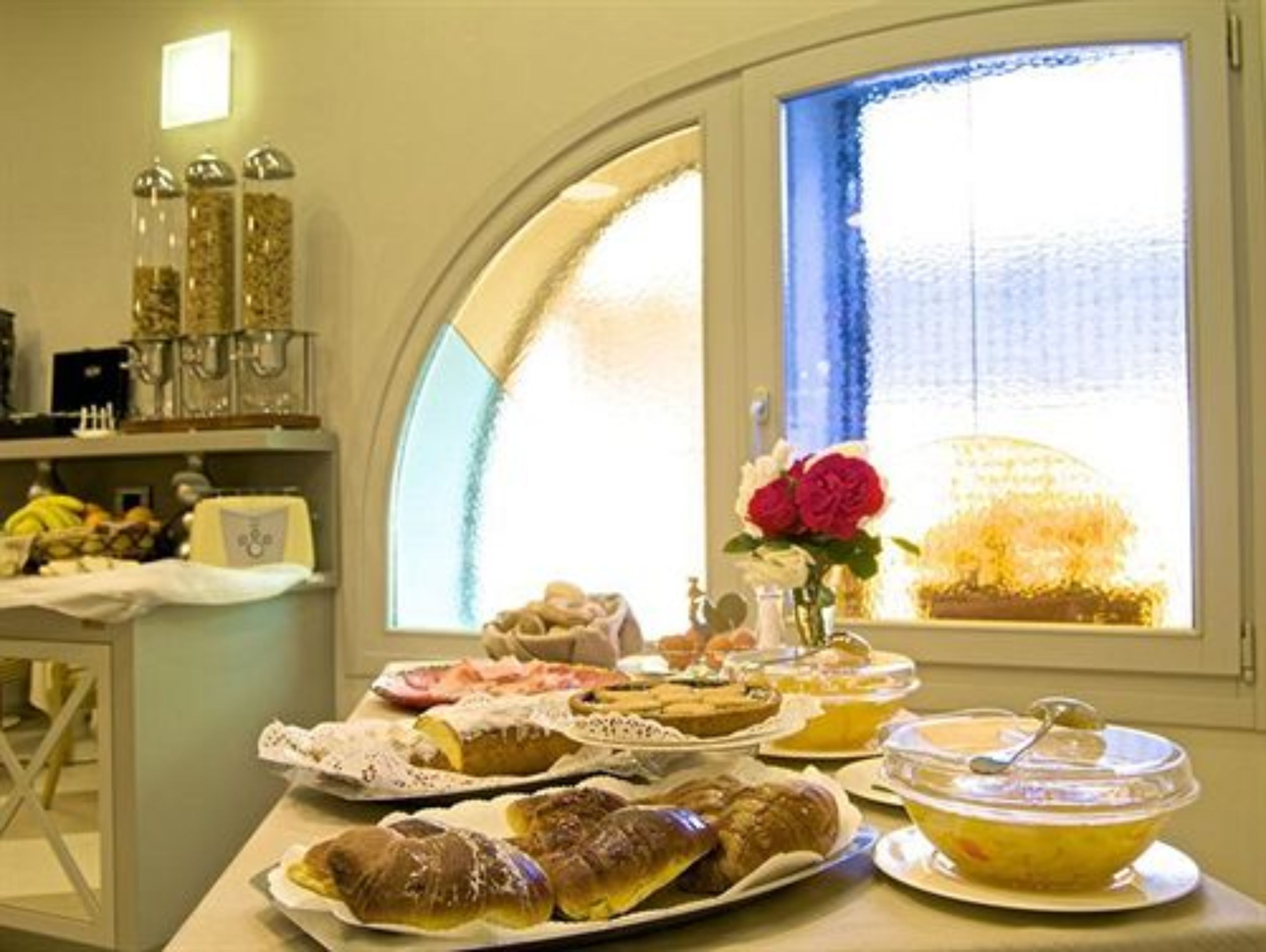 Um buffet de café da manhã com doces, um vaso com flores e uma janela com vista.