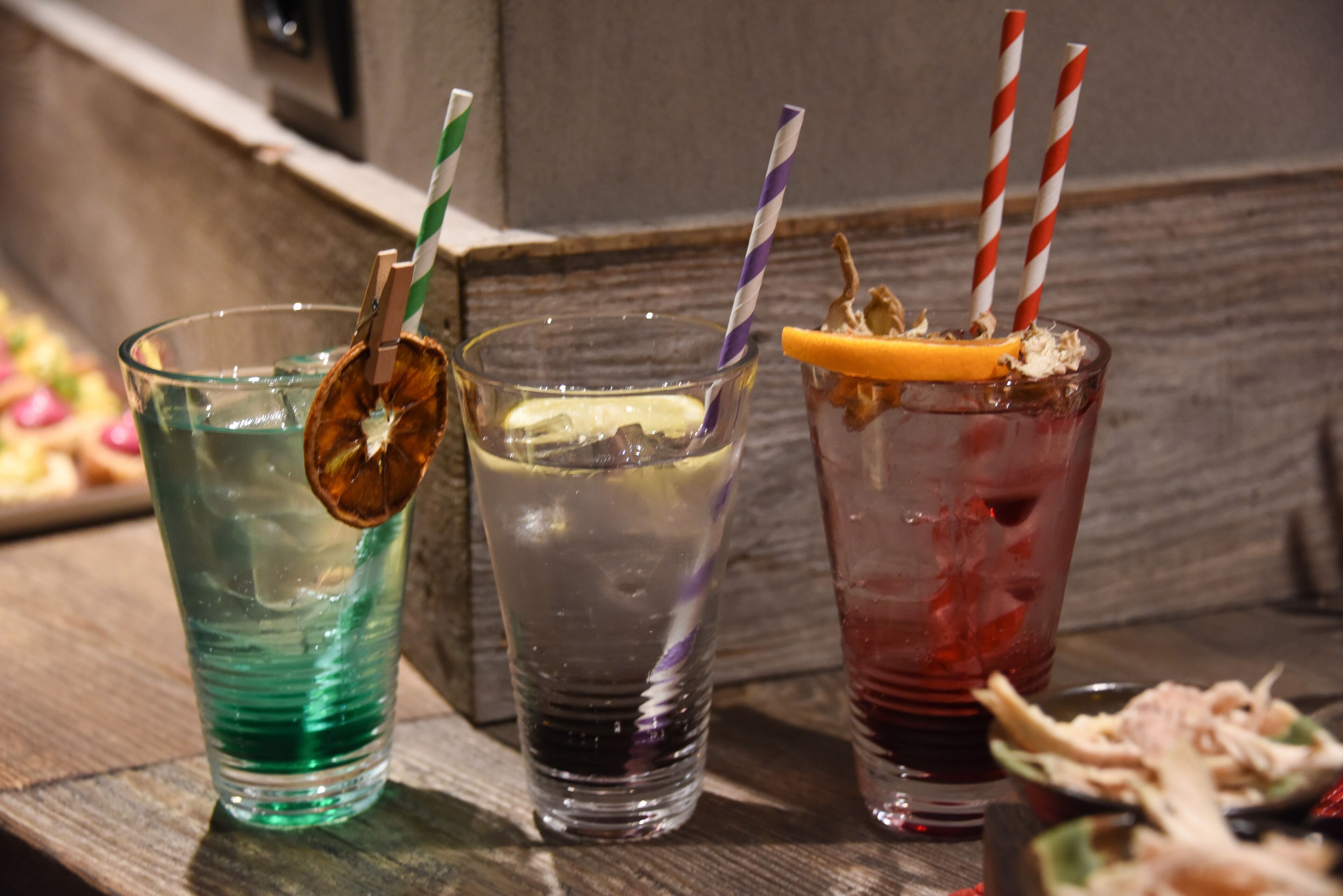 Três copos com bebidas de cores diferentes sobre uma superfície de madeira.