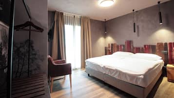 Quarto moderno com uma cama grande, uma cadeira, um cabideiro e vista para árvores pela janela.