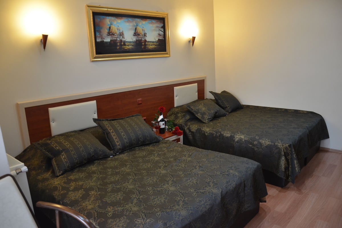Quarto de hotel com duas camas, um quadro na parede e uma mesa de cabeceira com uma garrafa e uma flor.