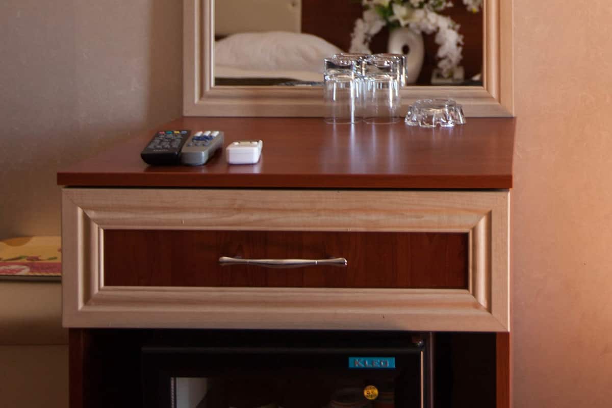 Um minibar com uma televisão acima, um espelho e um pequeno frigorífico abaixo.