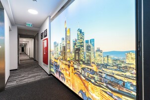 Um corredor com um mural da paisagem urbana na parede, um detector de incêndio e piso coberto por carpete.