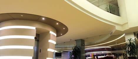 Um hall amplo com teto curvo, balcão de recepção, áreas de estar e escadaria para um andar superior.