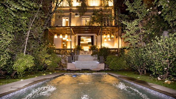 Um edifício bem iluminado com piscina na frente, rodeado por vegetação.