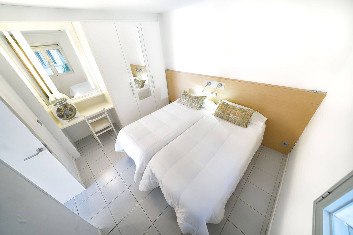 Quarto com duas camas, uma mesa de cabeceira, um espelho e uma janela.