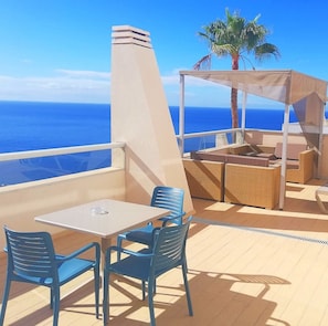 Um terraço com mesa e cadeiras, uma área de estar coberta e vista para o oceano.