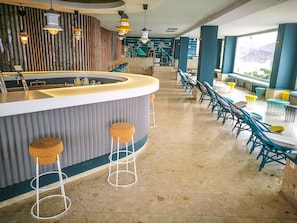 Uma área de bar moderna com balcão curvo, banquetas e um espaço de estar com mesas e cadeiras.
