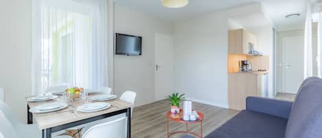 Uma sala moderna, com área de refeições, cozinha e televisão fixada na parede.