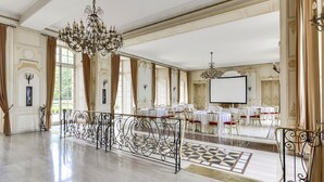 Uma sala de baile imponente com lustres, uma tela grande e mesas montadas para um evento formal.