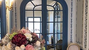Quarto com uma porta azul grande, piso de madeira e um vaso de flores sobre uma mesa.