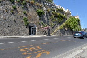 Uma rua com um muro de pedra e uma placa com a inscrição 'L'APPRODO'.
