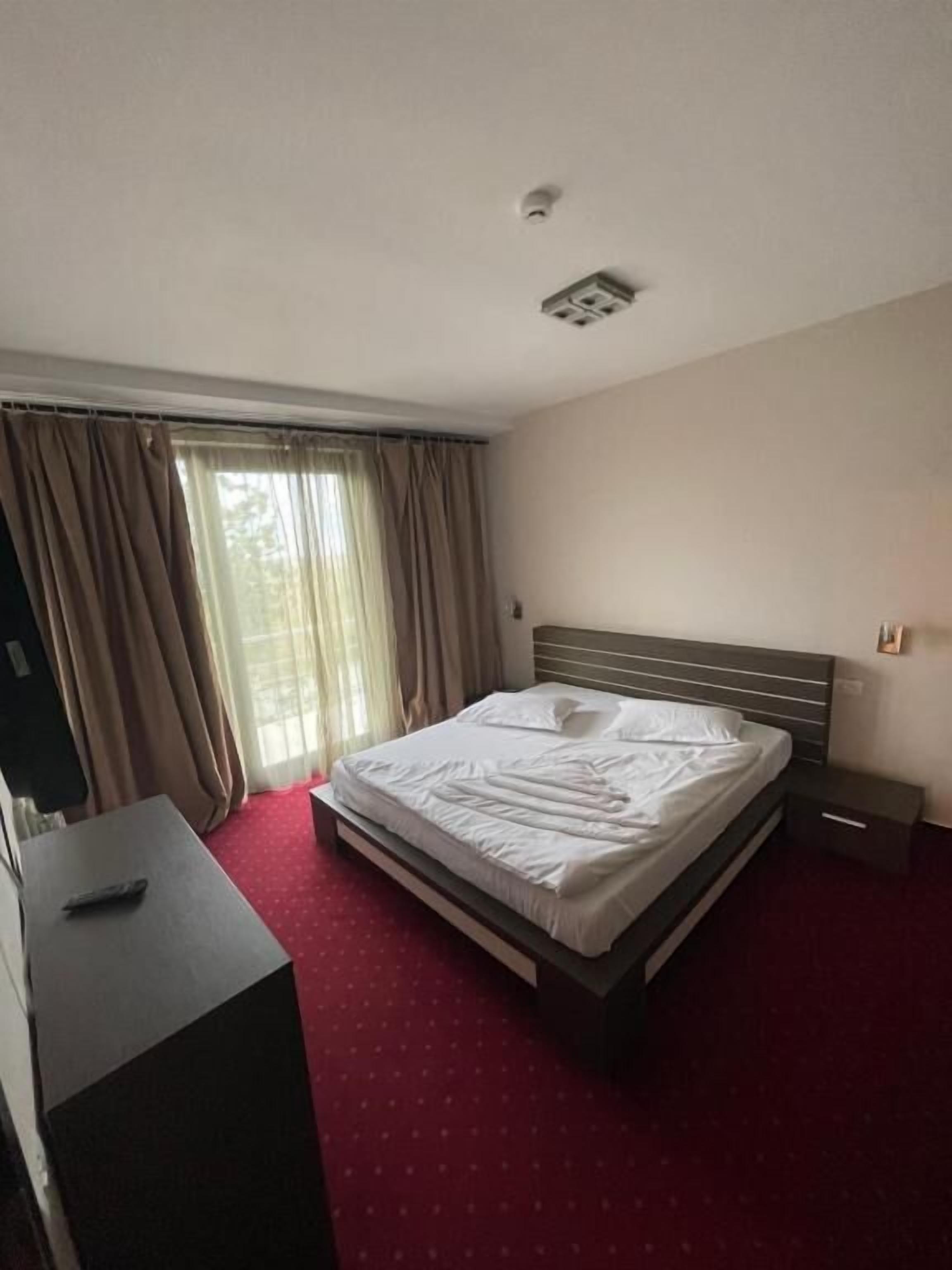 Quarto de hotel com cama, escrivaninha e janela com cortinas.