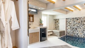 Uma casa de banho moderna com parede de pedra, lavatório embutido, frigorífico pequeno e banheira.