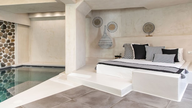 Quarto moderno com piscina integrada, parede de pedra e cama com almofadas estampadas.