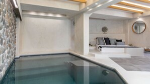 Uma área de spa com piscina em ambiente envidraçado, cama com cabeceira e espelho redondo na parede.