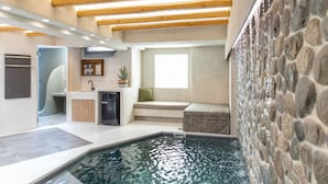 Uma piscina interior com parede de pedra e vigas de madeira.