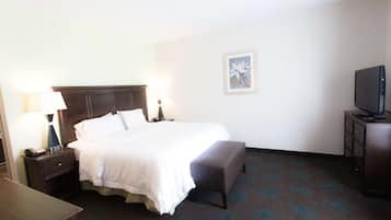 Quarto de hotel com cama, luminárias de cabeceira, televisão, um banco e um tapete com padrão floral.