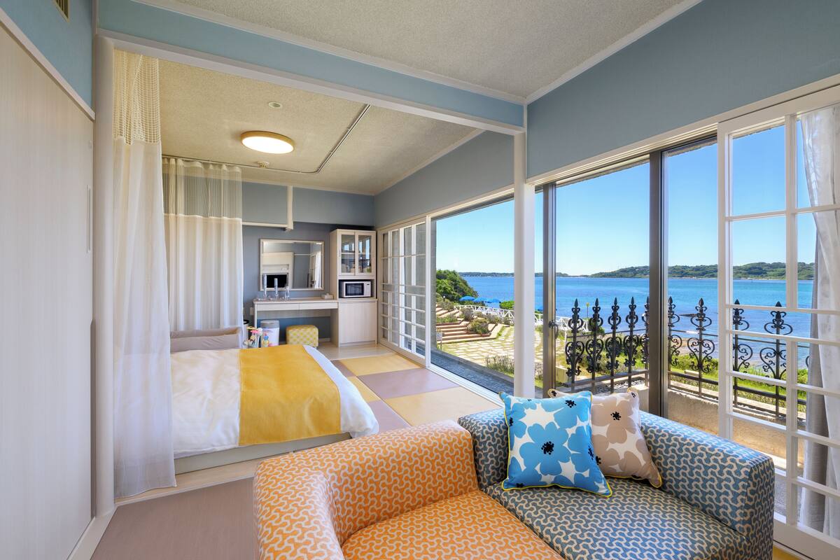 Quarto com cama, sofá e vista para o mar.