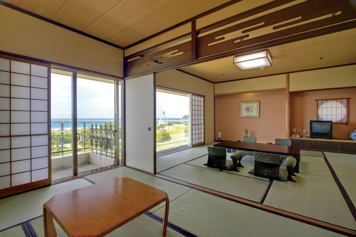 Um quarto japonês tradicional com tatames, uma mesa baixa, um sofá e uma televisão.