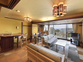 Quarto de hotel com varanda, área de refeições, sofá e televisão.