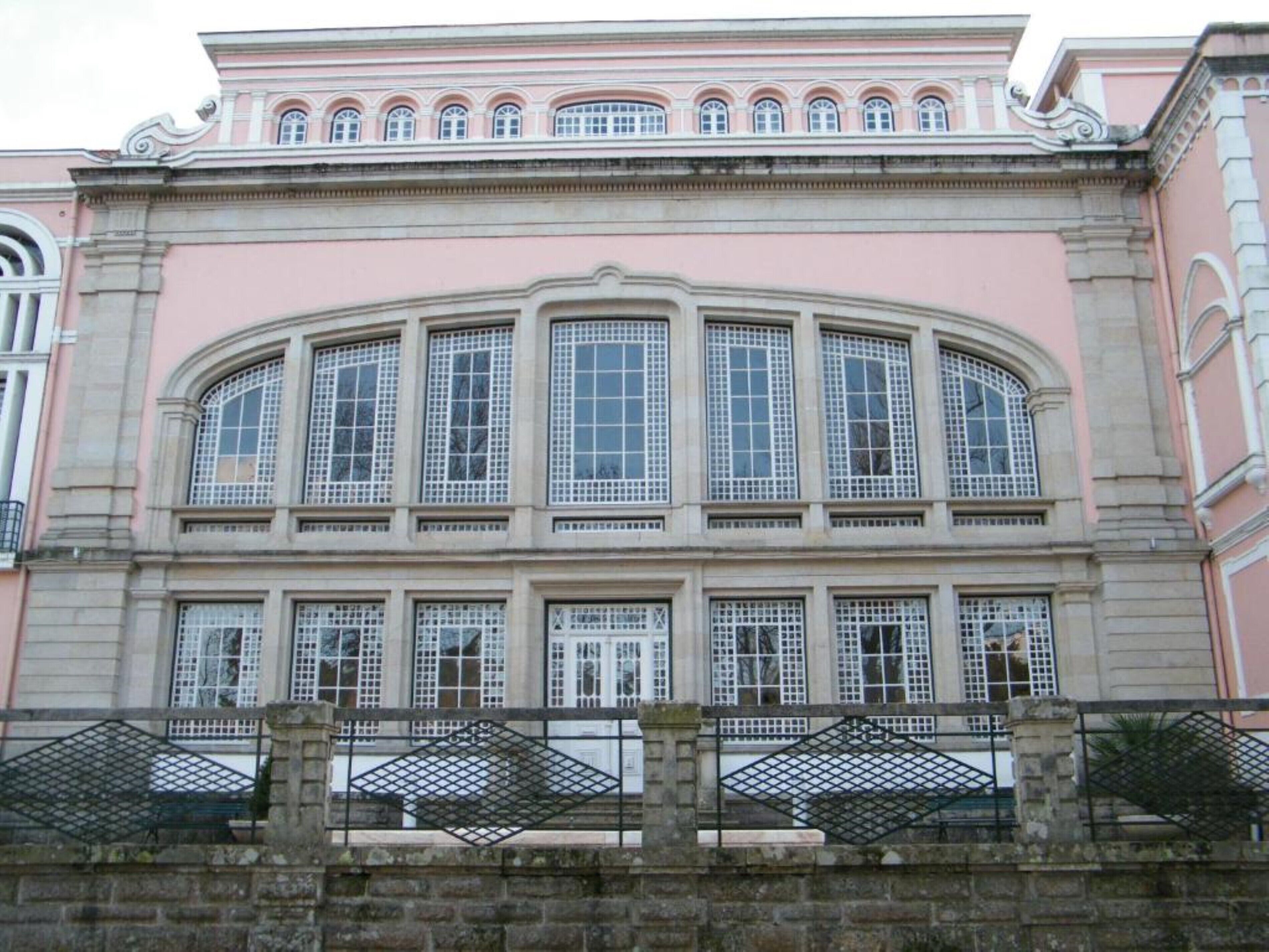 Um edifício rosa com grandes janelas em arco e fachada simétrica.
