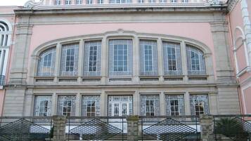 Um edifício rosa com grandes janelas em arco e fachada simétrica.