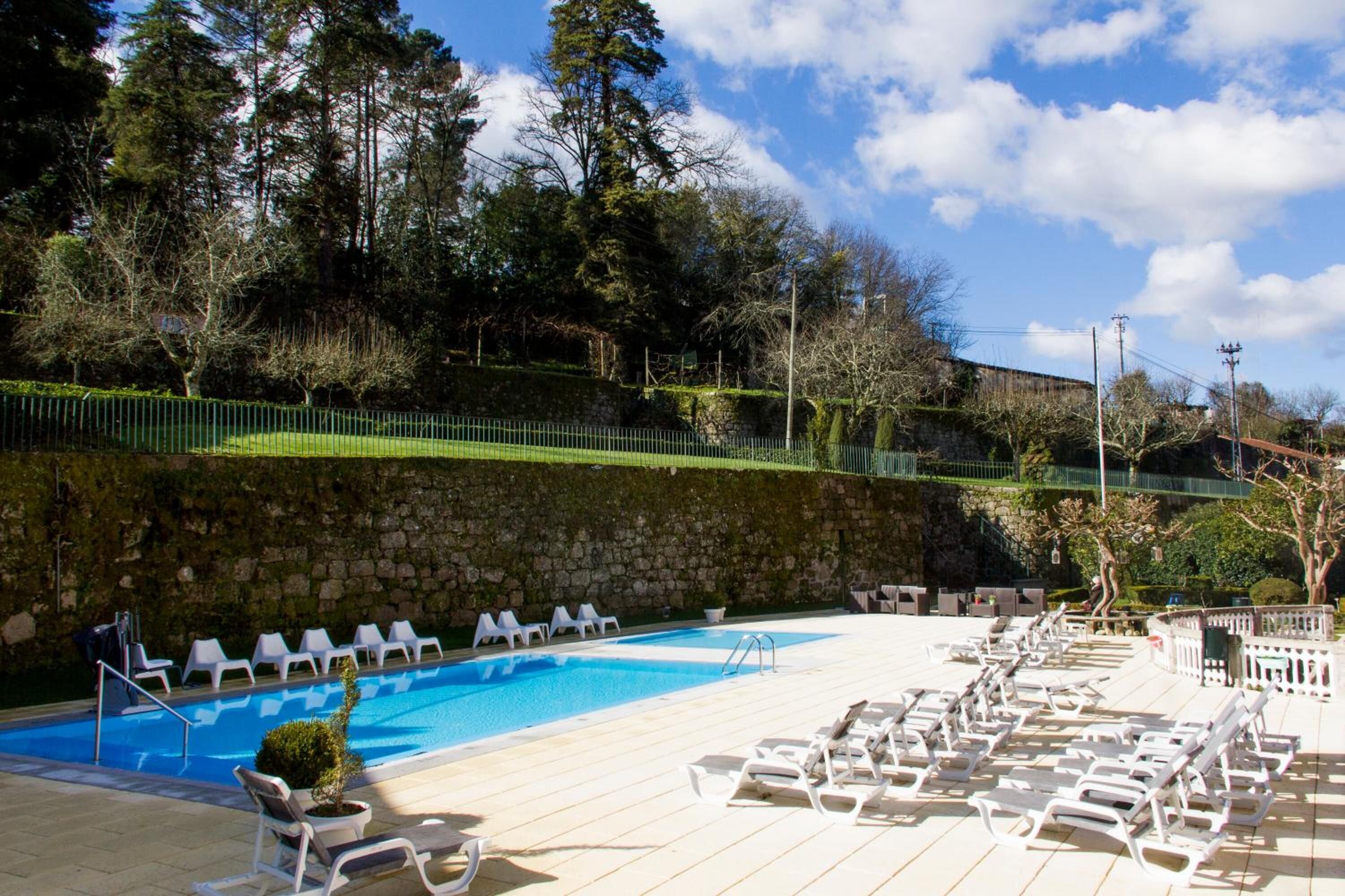 Piscina com espreguiçadeiras e um muro de pedra.