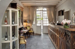 Um quarto com balcão de madeira, uma mesa de jantar com cadeiras, um lustre e uma grande janela com cortinas.