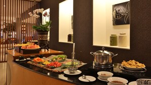 Um buffet com diversos pratos, uma panela quente e uma orquídea decorativa.