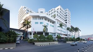 Um hotel moderno de vários andares com fachada branca, grandes janelas e uma entrada imponente com uma bandeira.