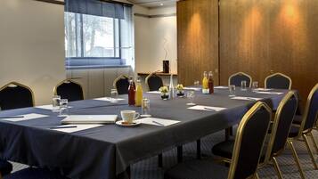 Uma sala de conferências com uma mesa comprida, cadeiras e diversos objetos, como copos, garrafas e papéis.