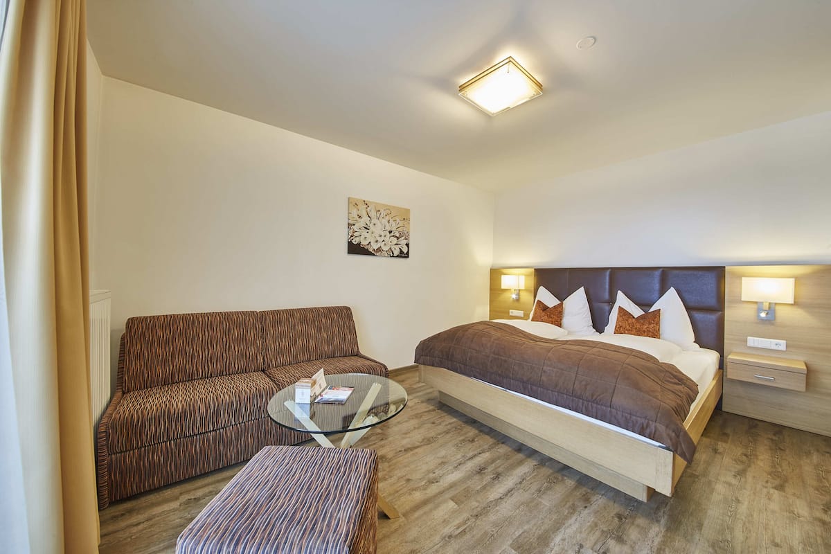 Quarto de hotel com cama, sofá, mesa redonda pequena e mesa de cabeceira com abajur.