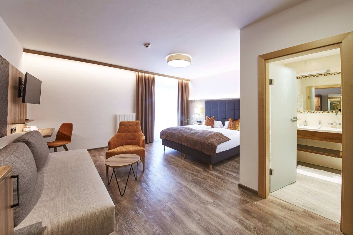 Quarto de hotel moderno com cama, sofá, escrivaninha e televisão.