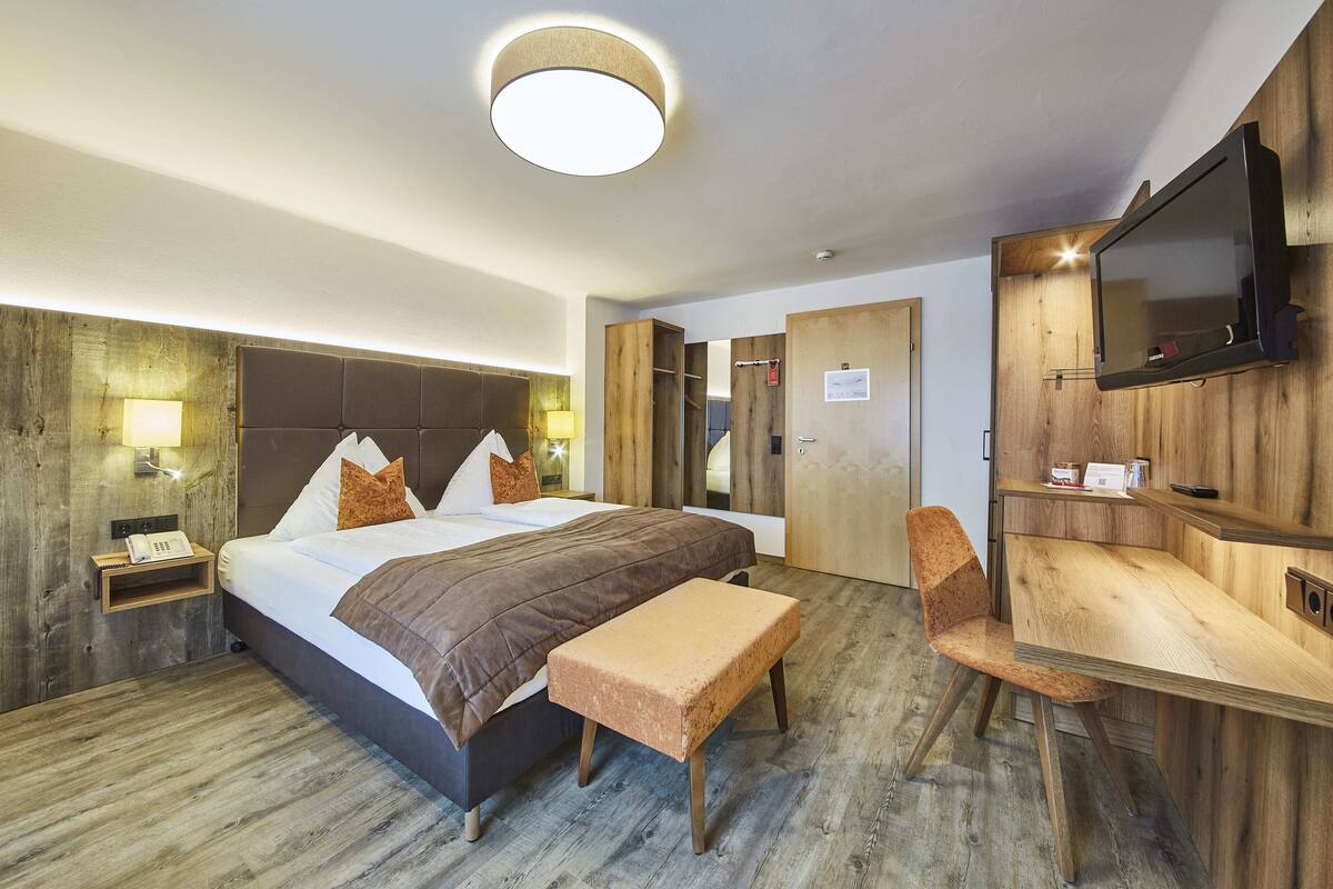 Quarto de hotel moderno com uma cama grande, uma escrivaninha de madeira, uma televisão e uma mesinha.
