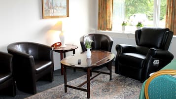 Um quarto com uma mesa de madeira redonda, duas poltronas de couro, uma pequena mesa lateral com um abajur e um vaso com flores.