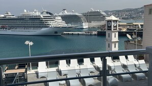 Uma área de piscina com espreguiçadeiras e vista para navios de cruzeiro atracados no porto.