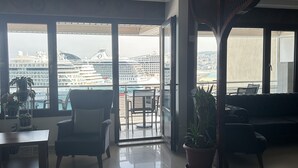 Ampla sala de estar com vista para um navio de cruzeiro, varanda com mobiliário externo e design de interiores moderno.